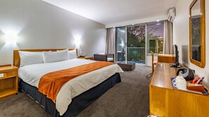 Quarto de hotel com uma cama grande, uma escrivaninha com chaleira, uma cadeira e vista para o exterior através de uma porta de vidro deslizante.