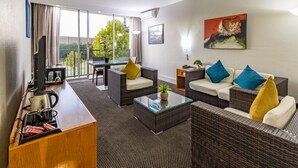 Quarto de hotel moderno com varanda, móveis de vime, mesa de centro de vidro e uma pintura de um leão.