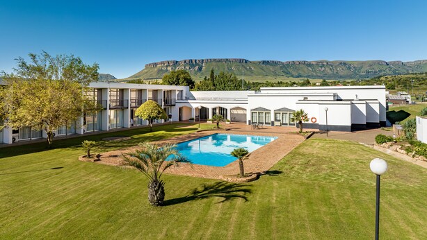 Um hotel moderno com piscina, gramado bem cuidado e vista para as montanhas.