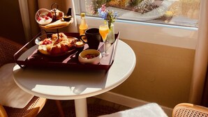 Bandeja de café da manhã com croissants, iogurte e suco em uma mesa perto de uma janela com vista para árvores e um corpo d'água.