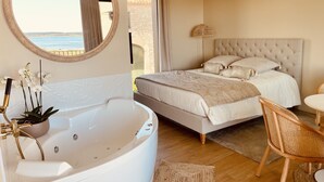 Quarto com cama grande, banheira, espelho redondo e vista para o mar.