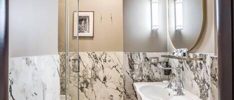 Um banheiro com pia de mármore, box de vidro e um quadro pendurado na parede.