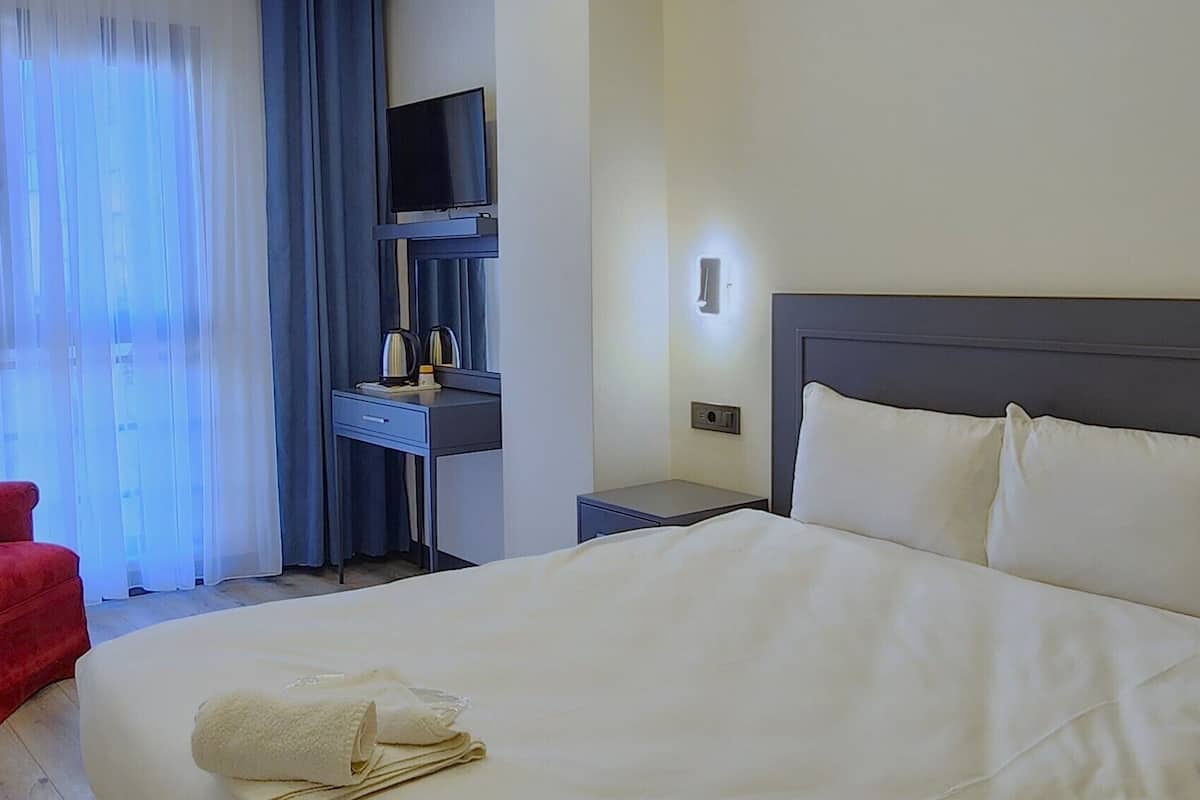 Quarto de hotel com uma cama, poltrona vermelha, escrivaninha e televisão de tela plana.