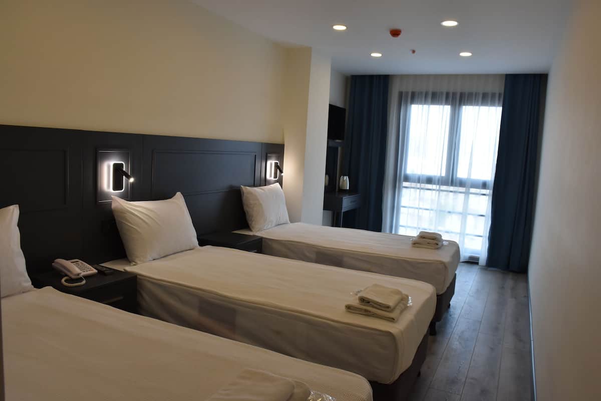 Quarto de hotel com três camas de solteiro, telefone ao lado da cama e televisão na parede.