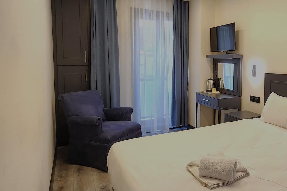 Quarto de hotel com cama, cadeira, televisão, máquina de café e janela com cortinas.