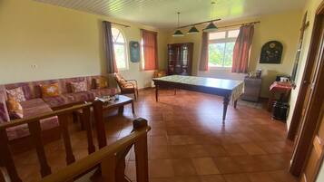 Ampla sala de estar com sofá, mesa de jantar e cozinha equipada com geladeira e pia.