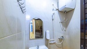 Casa de banho com lavatório, espelho, porta-toalhas, chuveiro e dispensador de sabonete.