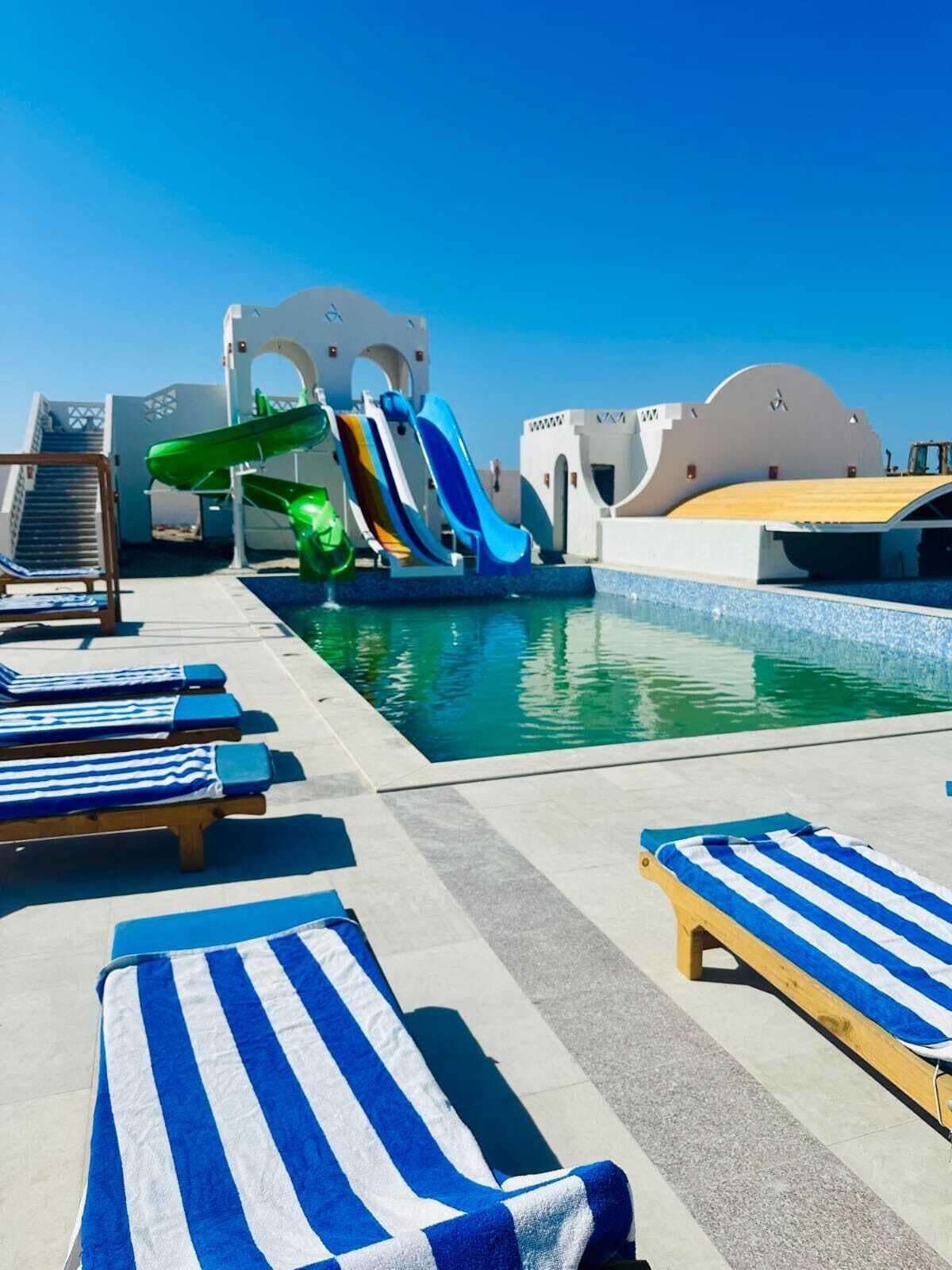 Uma área de piscina com espreguiçadeiras, um toboágua e um céu azul límpido.