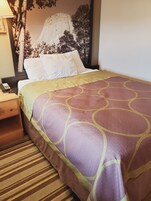 Quarto de hotel com uma cama, mesa de cabeceira com telefone e luminária de parede.