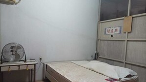 Quarto pequeno com uma cama de solteiro, escrivaninha e ventilador.