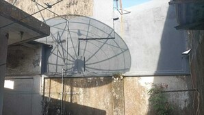 Um edifício de concreto com antena parabólica, um pequeno vaso de planta e um poste de metal.