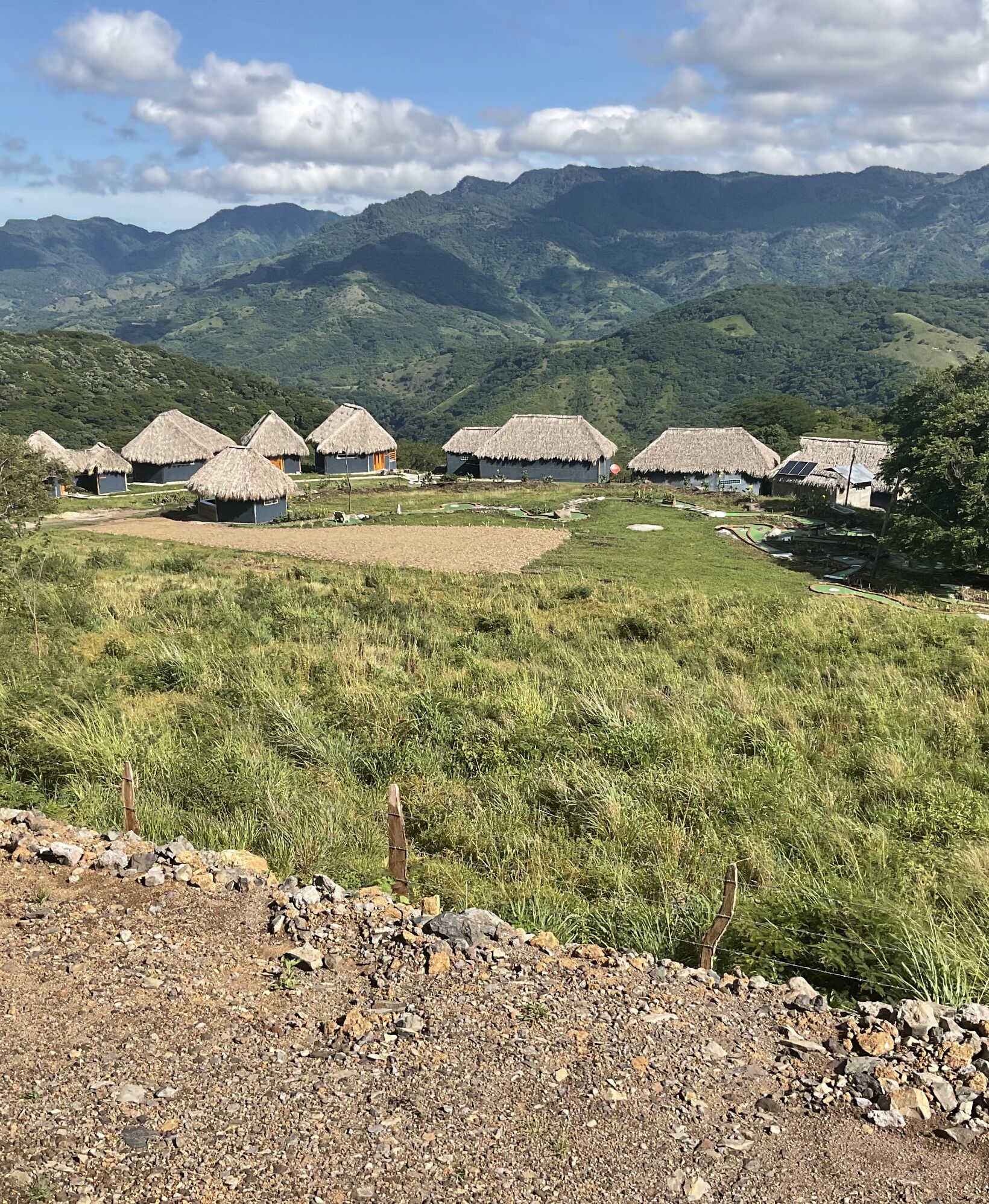 Uma vila rural com casas de telhado de palha e montanhas ao fundo.