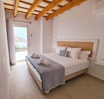Quarto com cama, janela com cortinas e estrutura de teto em madeira.