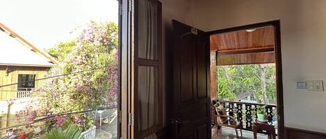 Quarto com teto de madeira, uma grande janela com vista para uma varanda e uma porta que dá para o exterior.