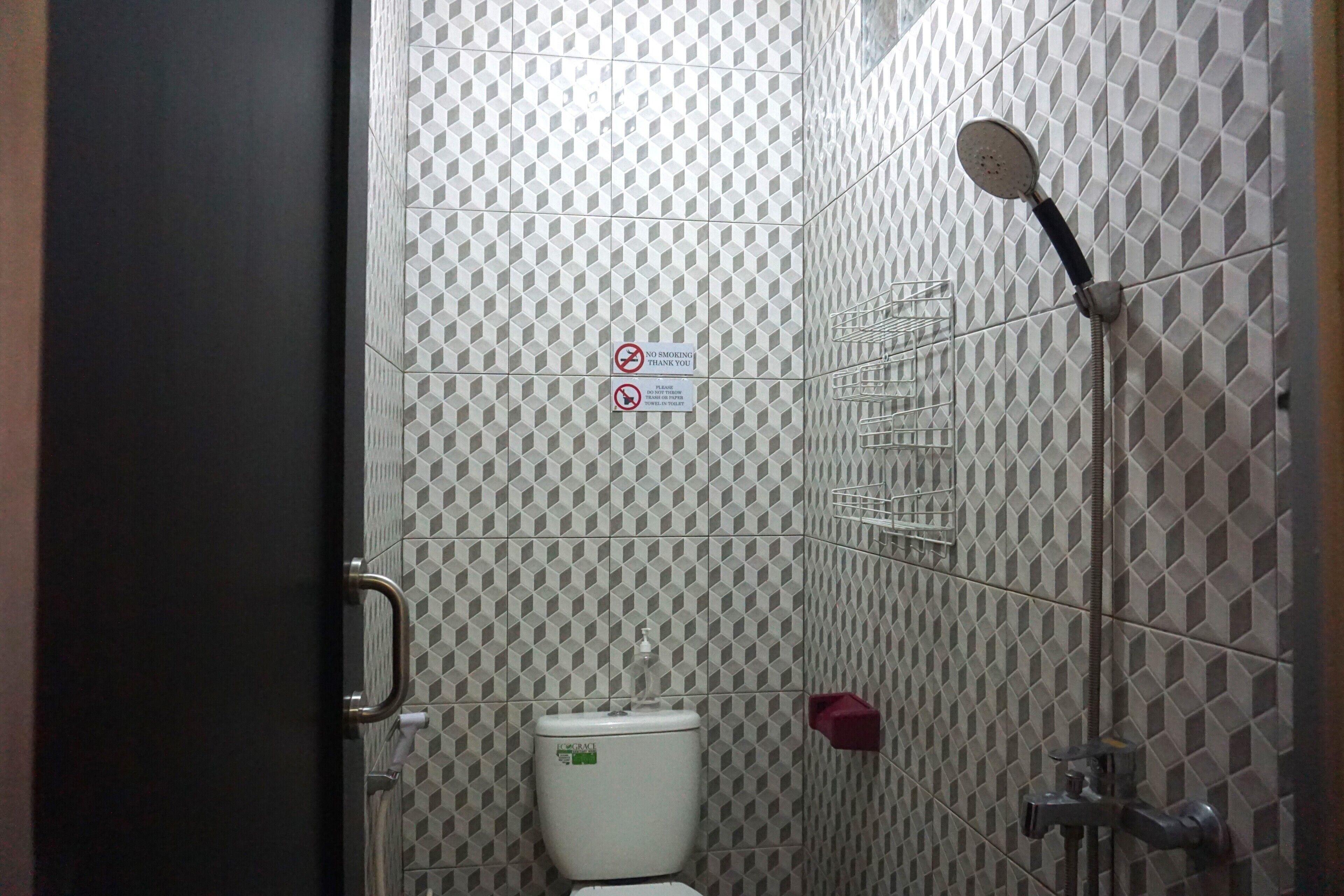 Casa de banho com sanita, chuveiro com chuveiro manual e placa de proibido fumar na parede.