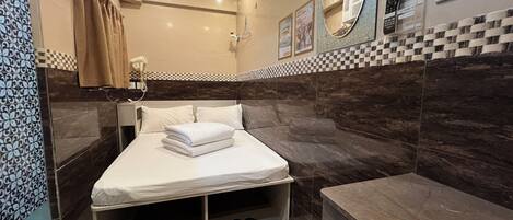 Quarto de hotel com cama, um banco, um espelho e painel de controlo fixado na parede.