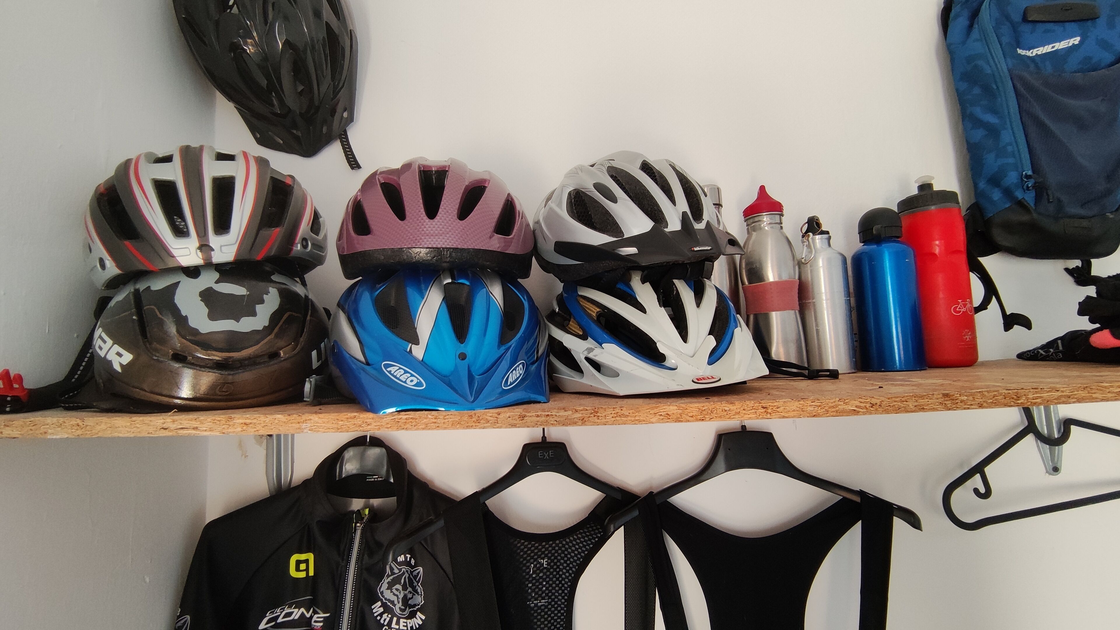 Uma prateleira com vários capacetes, garrafas de água e uma mochila.