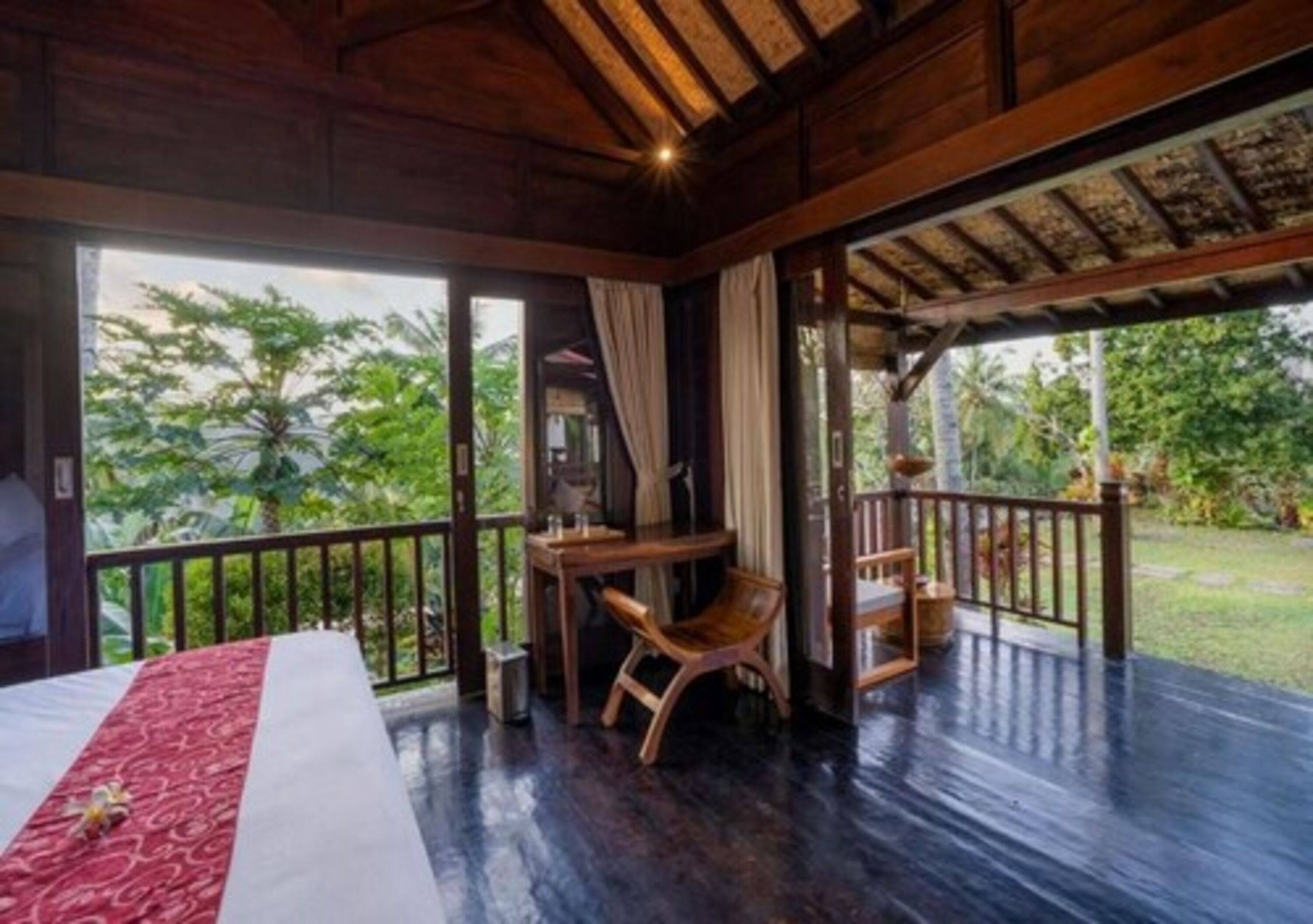 Quarto de madeira com uma cama, escrivaninha e cadeira. Visão de vegetação lá fora.