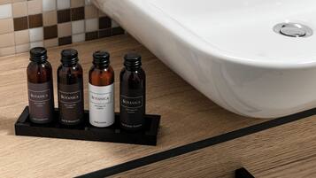 Um banheiro com pia branca, espelho e painel de azulejos. Quatro frascos de produtos de cuidados Botanica estão no balcão.