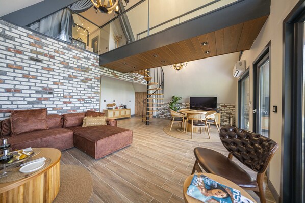 Uma sala de estar moderna com parede de tijolo, teto de madeira, escada, televisão e área de jantar.
