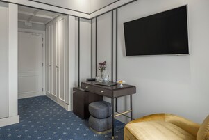 Quarto de hotel com escrivaninha, televisão, cadeira e carpete estampado.