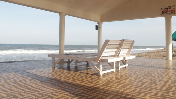 Uma área de praia coberta com piso de madeira, uma cadeira de praia branca e vista para o oceano.