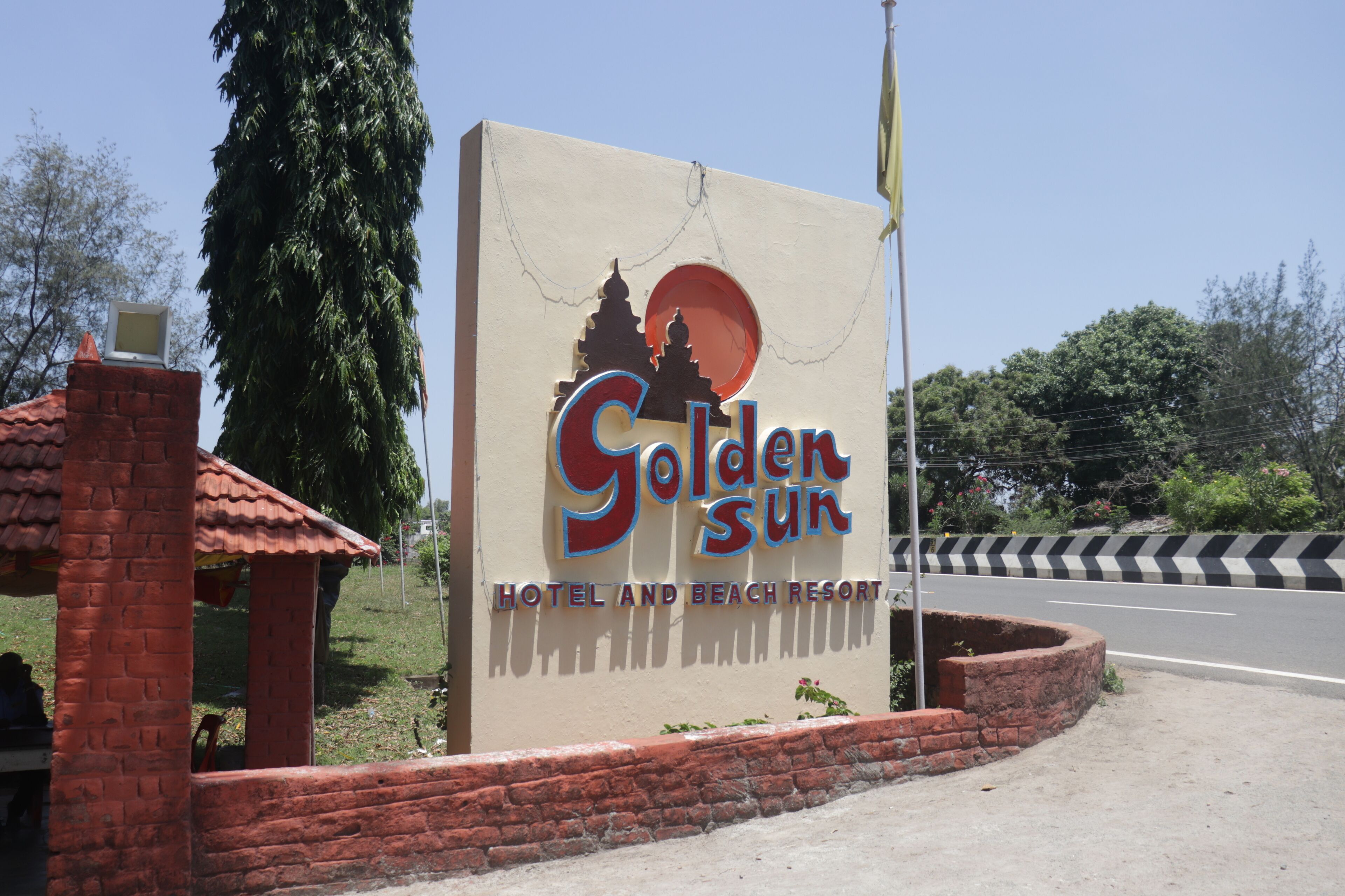 Placa para o Golden Sun Hotel e Beach Resort, com céu claro e uma estrada com guia demarcada em preto e branco.