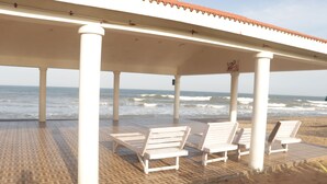 Um pavilhão à beira-mar com colunas brancas e piso de azulejos, com vista para o oceano.