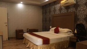 Quarto de hotel com uma cama grande, piso de madeira, escrivaninha, cadeira, mesa de cabeceira e ar condicionado.