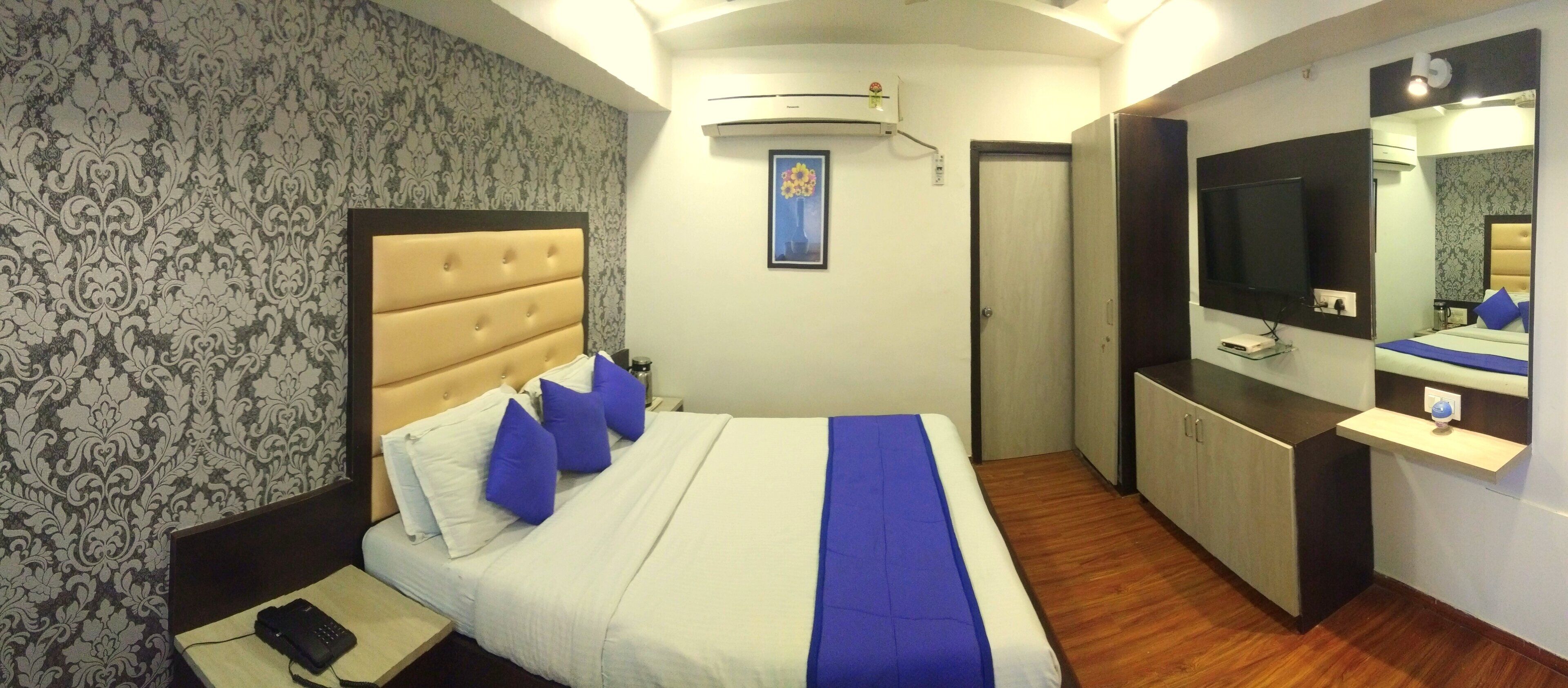 Quarto de hotel com cama, escrivaninha, guarda-roupa, televisão e ar condicionado.