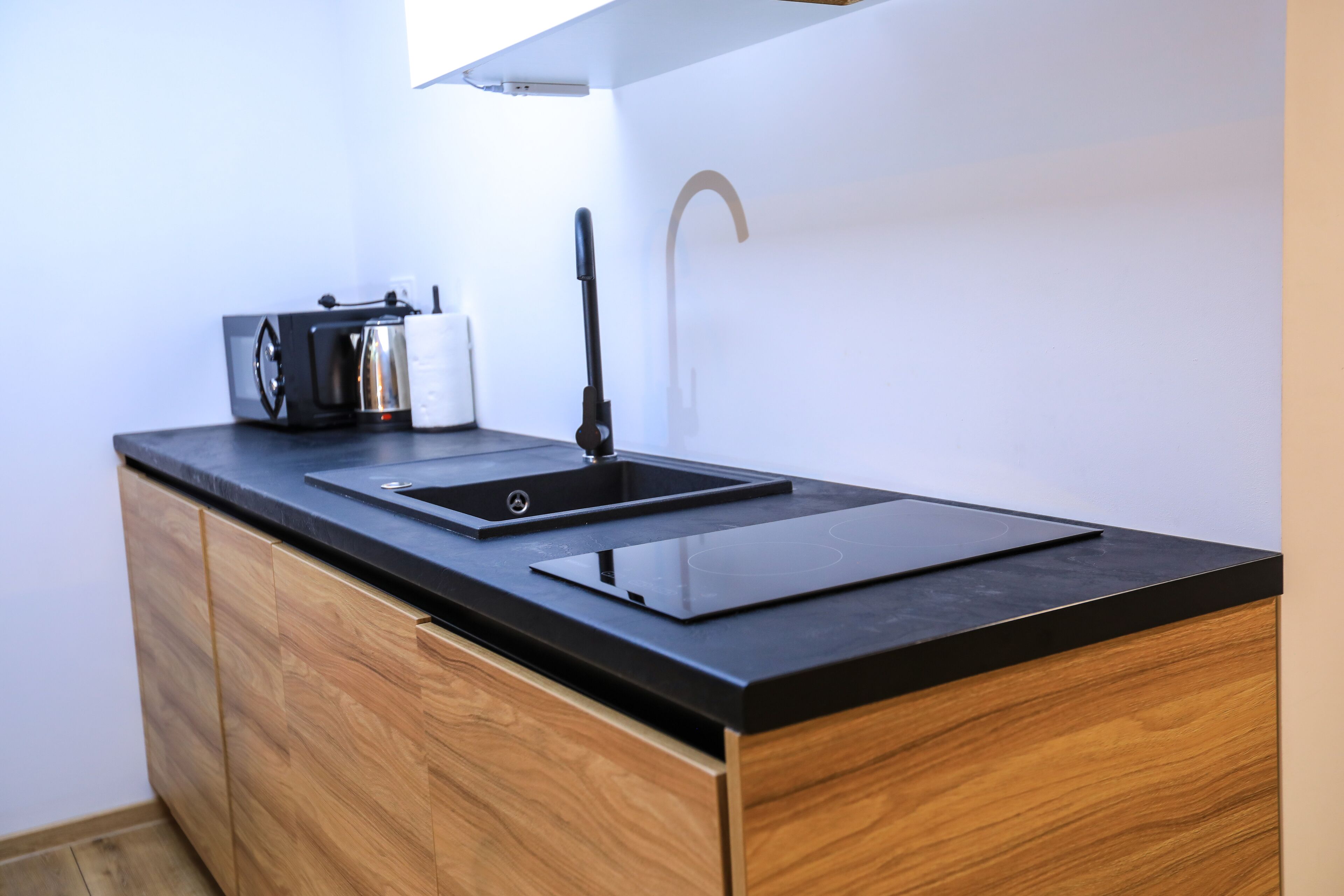 Cozinha moderna com bancada preta, pia e armários de madeira.