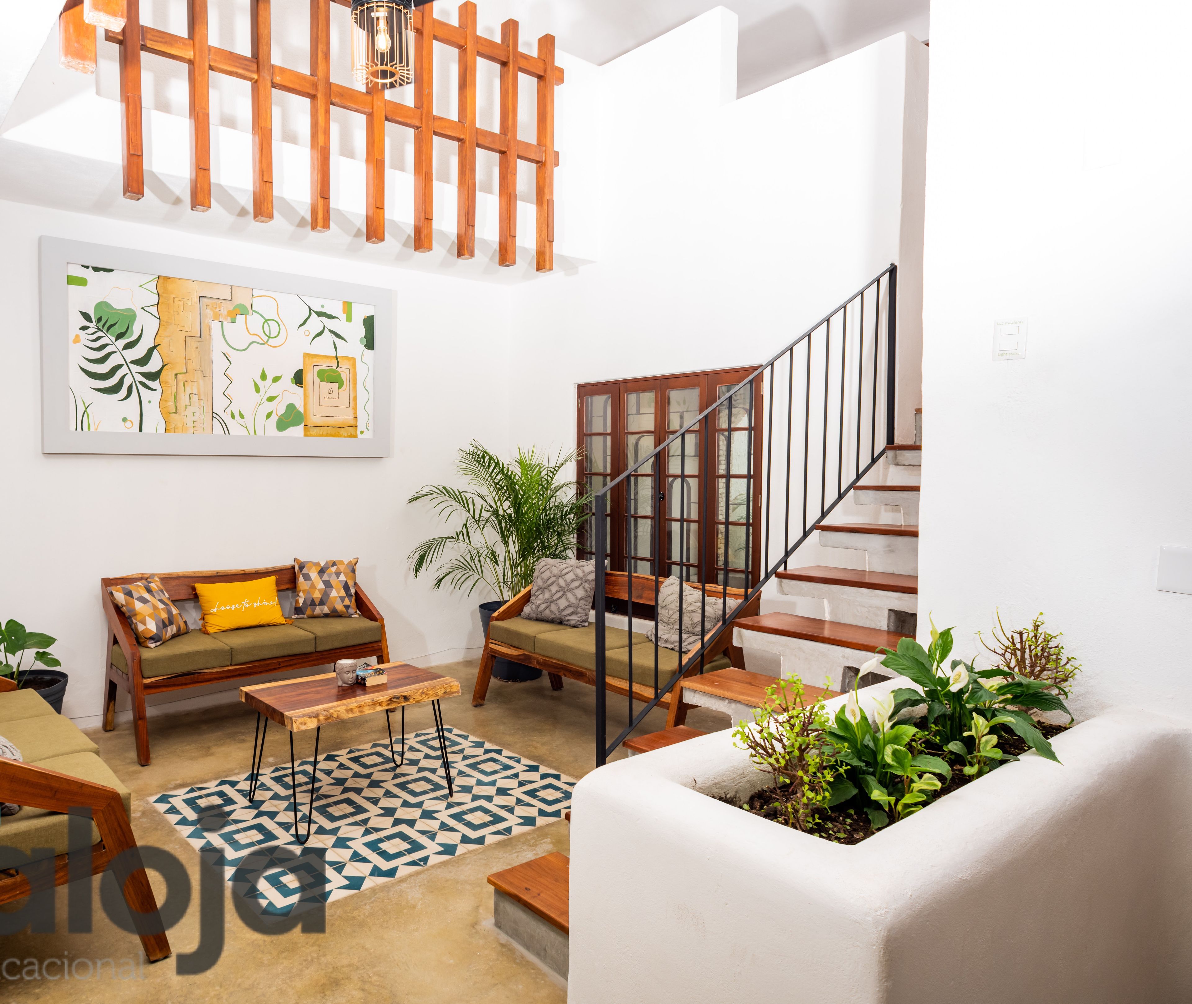 Ampla sala de estar com escada de madeira, sofás, mesa de centro e um grande quadro abstrato na parede.