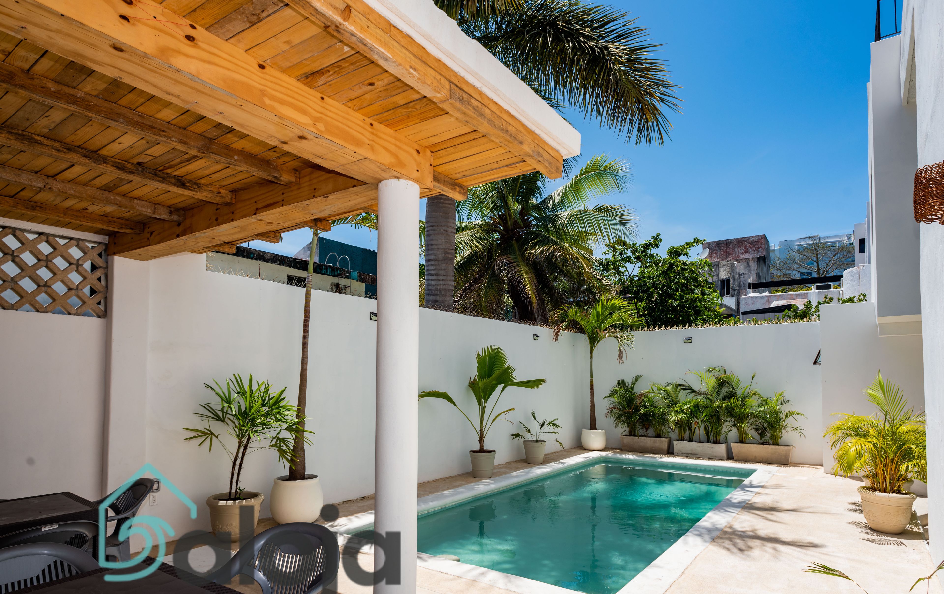 Uma área de piscina com pérgola de madeira, plantas em vasos e piscina azul cristalina.