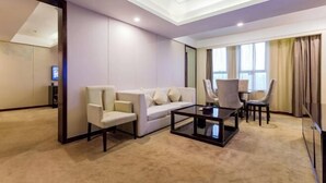 Quarto de hotel moderno com sofá, poltronas, mesa de centro e área de jantar com cadeiras e uma mesa.