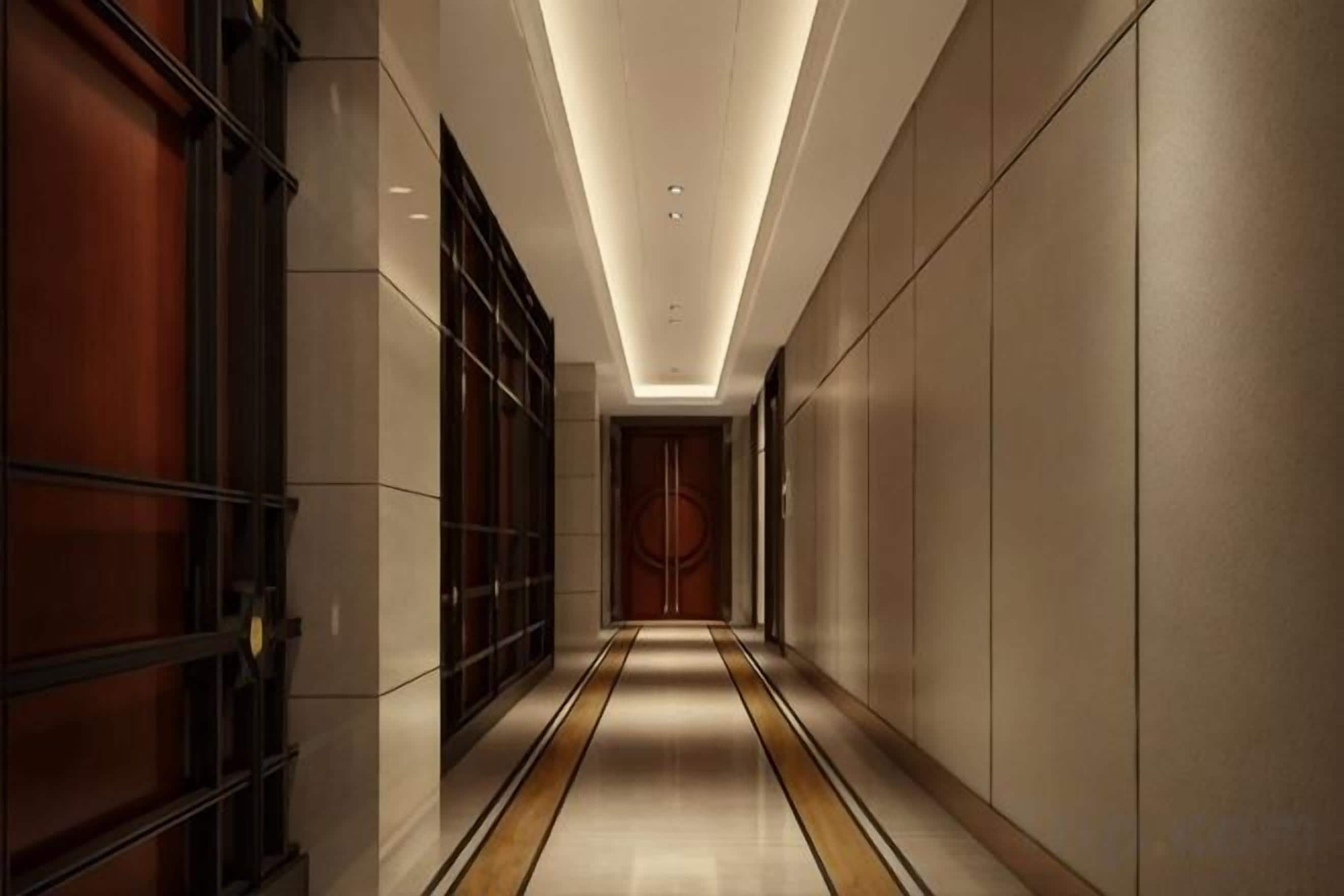 Corredor com porta de madeira no final, piso de azulejos e luminária moderna no teto.