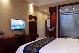 Quarto de hotel com cama, televisão, secretária com computador e guarda-roupa.