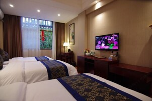 Quarto de hotel com duas camas, uma escrivaninha, uma televisão e uma janela com cortinas.