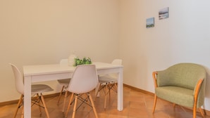 Uma área de refeições com uma mesa branca, quatro cadeiras e uma poltrona verde.