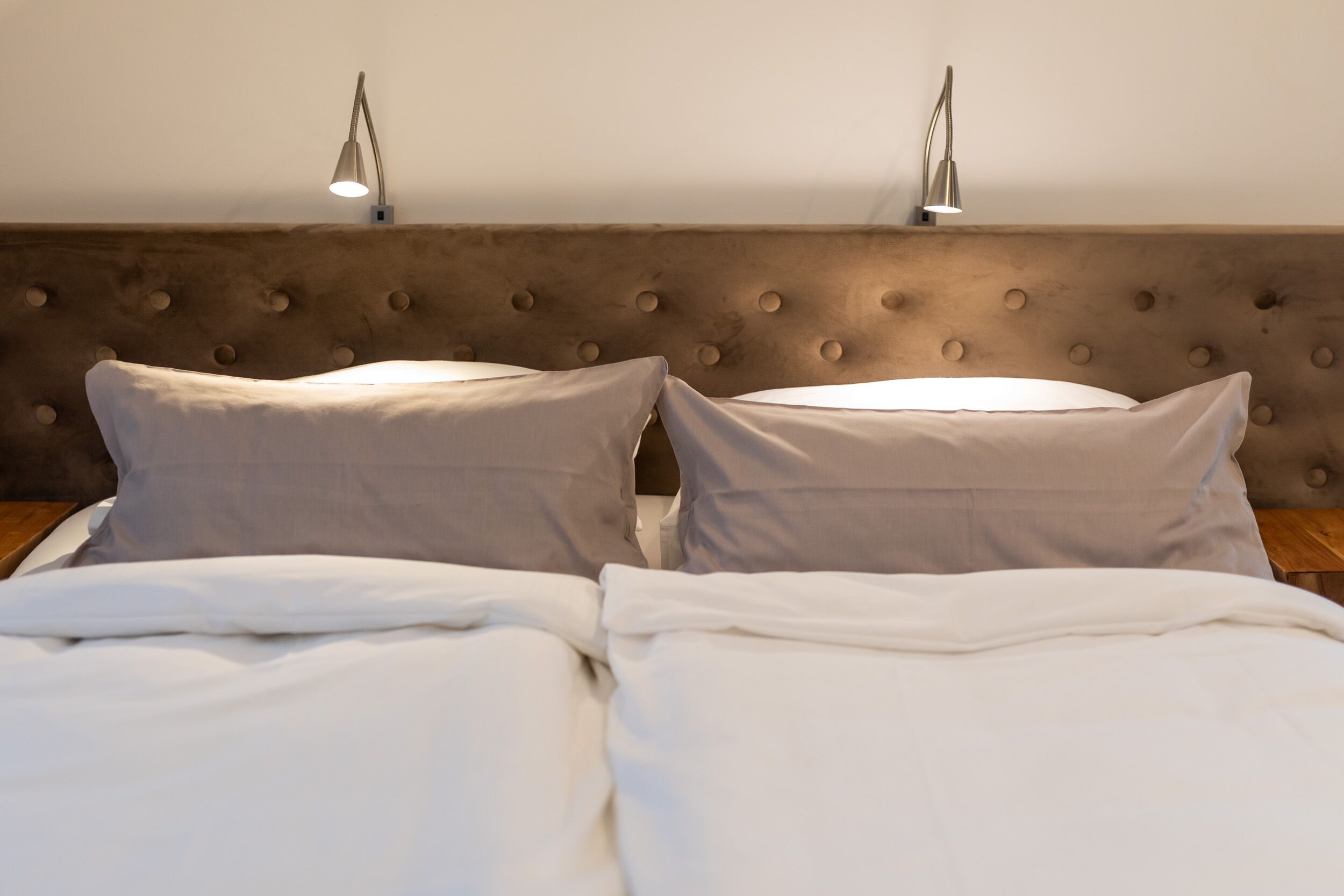 Uma cama com cabeceira estofada, duas luminárias de cabeceira e roupa de cama branca.