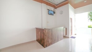 Uma área de recepção com um balcão de madeira, uma TV na parede e um relógio.