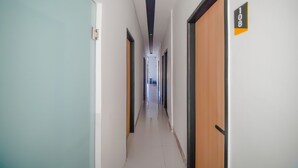 Um corredor comprido e estreito com portas em ambos os lados, que leva a um quarto luminoso no final.