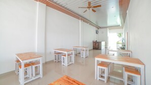 Um quarto espaçoso com paredes brancas, piso de madeira e várias mesas brancas com bancos.