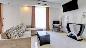 Uma sala de estar moderna com sofá, mesa de centro, TV fixada na parede e mesa lateral com abajur.