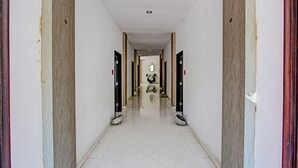 Um corredor com chão de azulejos, painéis de madeira nas paredes e portas com molduras pretas e detalhes vermelhos.