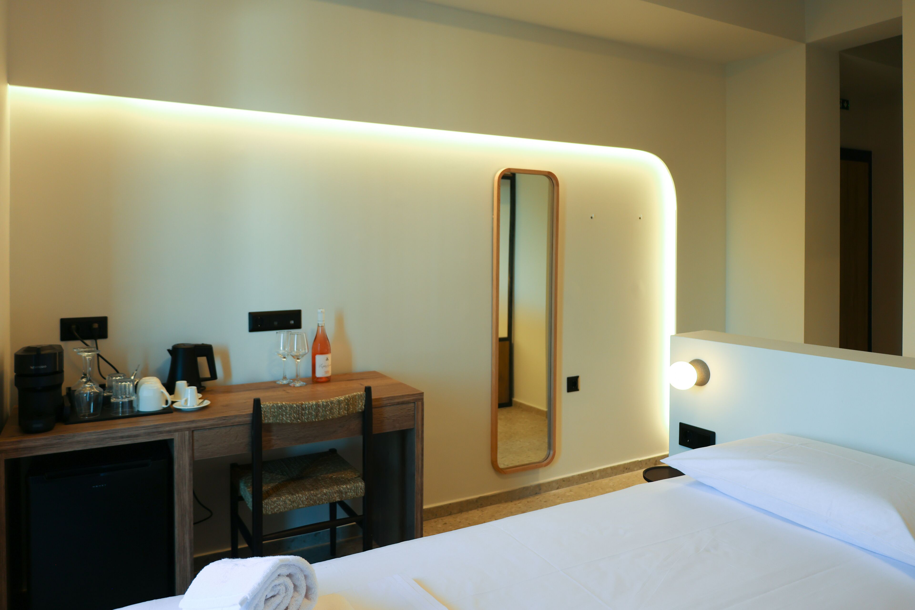 Quarto de hotel com cama, escrivaninha e cadeira, cafeteira, taça de vinho e garrafa de vinho.