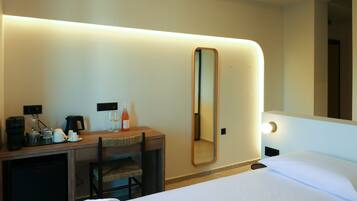 Quarto de hotel com cama, escrivaninha e cadeira, cafeteira, taça de vinho e garrafa de vinho.