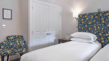 Quarto de hotel com uma cama, uma cadeira, um guarda-roupa e uma mesa de cabeceira com abajur.