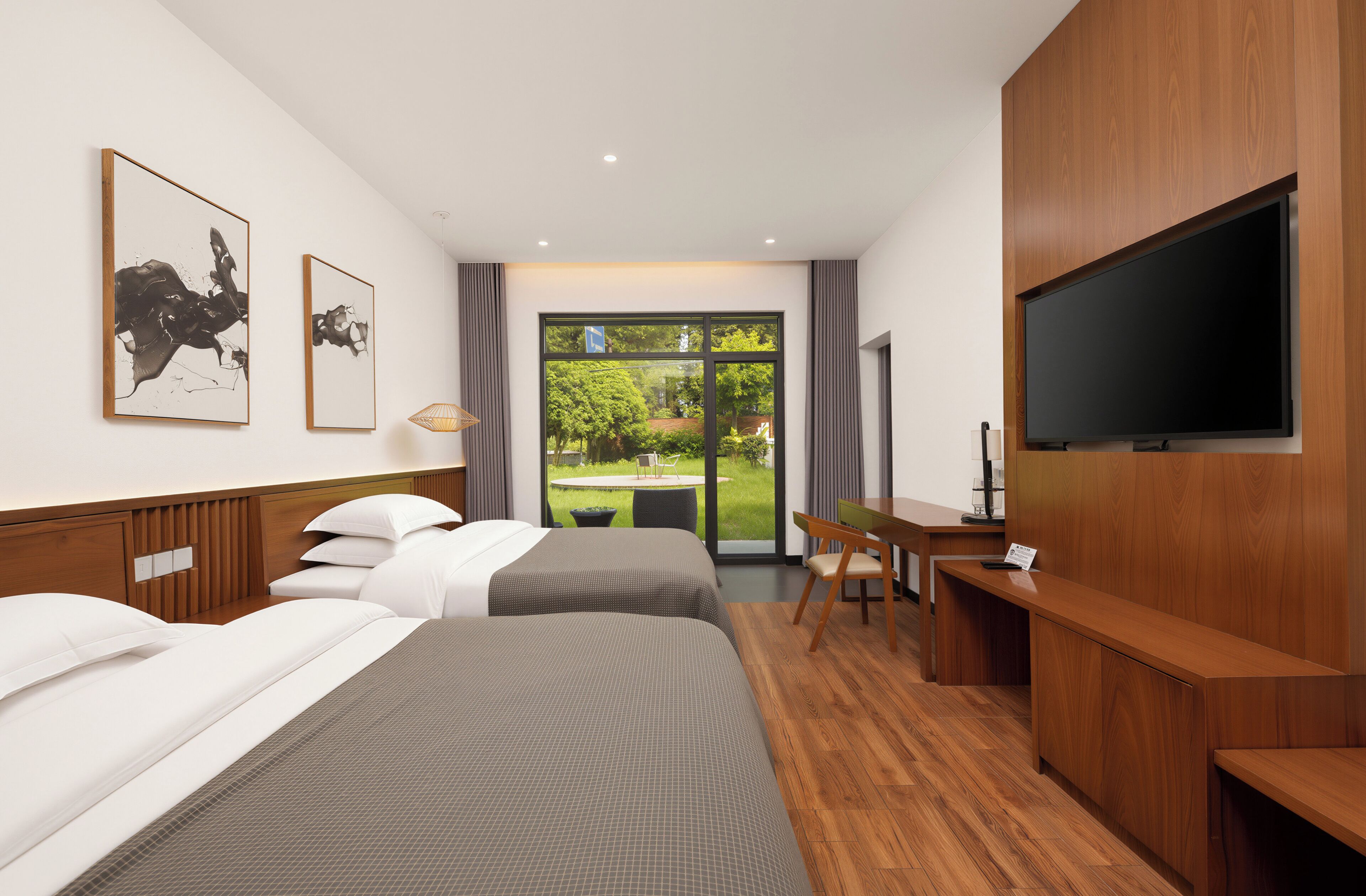 Quarto de hotel com duas camas, uma escrivaninha, televisão e uma janela grande com vista para o verde.
