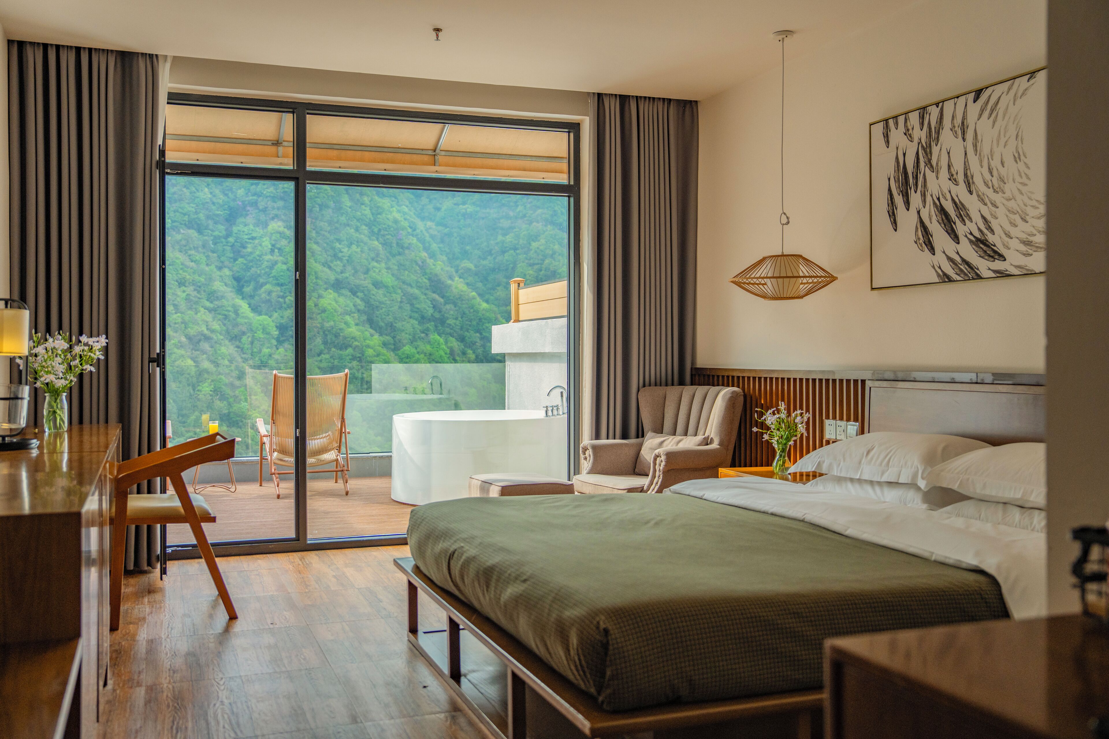 Quarto de hotel com uma cama, uma cadeira, uma escrivaninha, uma janela grande com vista para uma floresta e um quadro na parede.