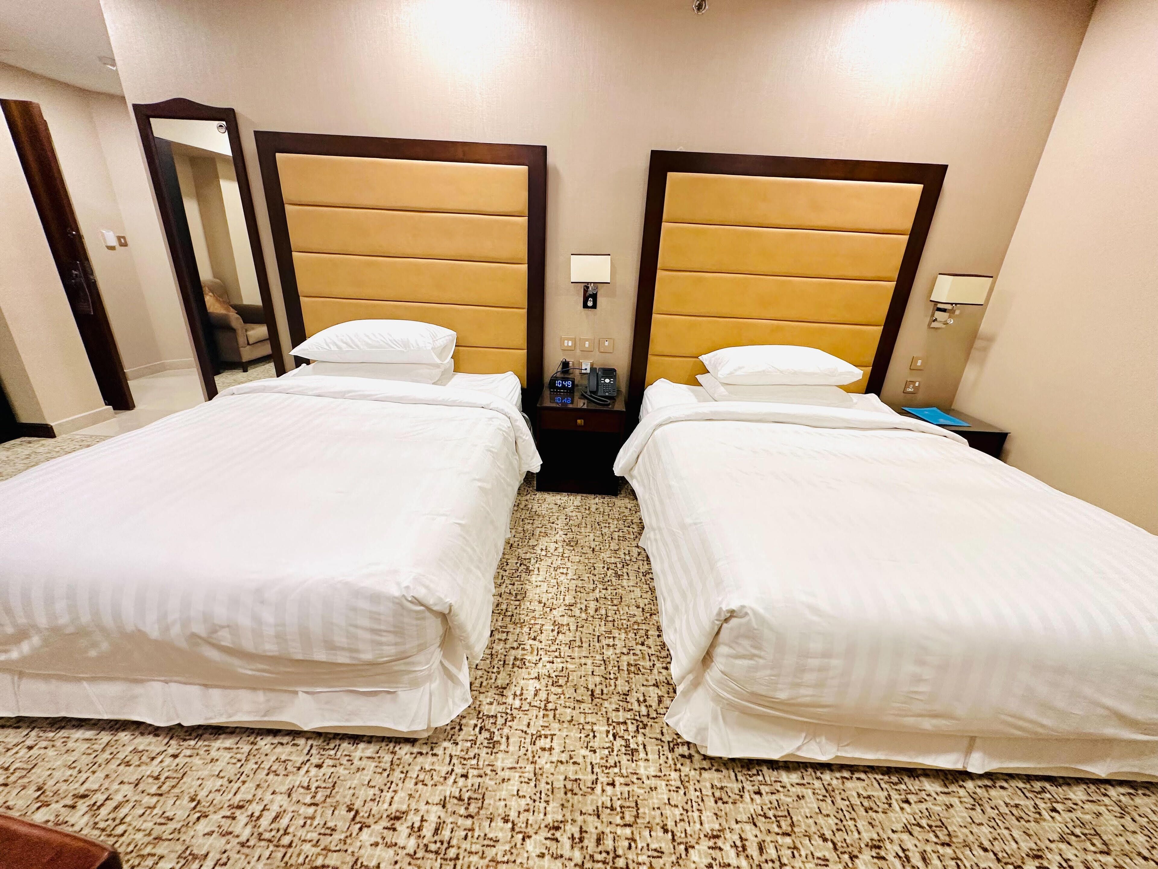 Quarto de hotel com duas camas, uma mesa de cabeceira com telefone e um espelho.